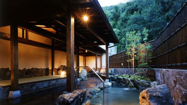 Um onsen japonês tradicional com banheira de pedra, estruturas de madeira e cerca de bambu.