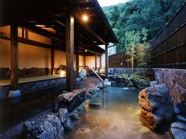 Um onsen japonês tradicional com banheira de pedra, estruturas de madeira e cerca de bambu.