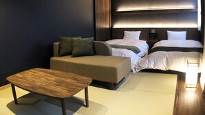 Quarto de hotel moderno com sofá, duas camas, uma mesinha e um ar condicionado.