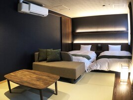 Quarto de hotel moderno com sofá, duas camas, uma mesinha e um ar condicionado.