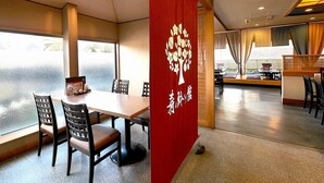 Um restaurante com uma janela grande, um letreiro vermelho com caracteres chineses e uma mesa com cadeiras.