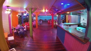 Um restaurante com chão de madeira, cadeiras coloridas e um balcão com vista para o mar.