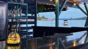 Uma área de bar com vista para um barco na água, prateleiras com garrafas e um abajur decorativo.