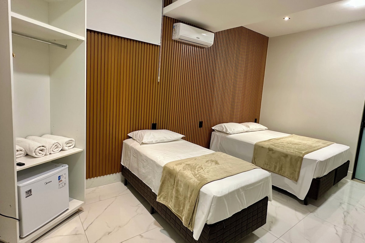 Quarto de hotel com duas camas, um minibar e um guarda-roupa.
