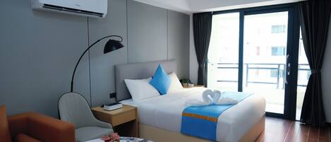 Quarto de hotel com cama, escrivaninha, cadeira, mesa redonda com flores e uma grande janela com cortinas.