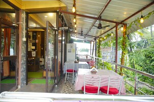 Uma área de recepção com uma placa, mesas com almofadas vermelhas e vista para o verde lá fora.