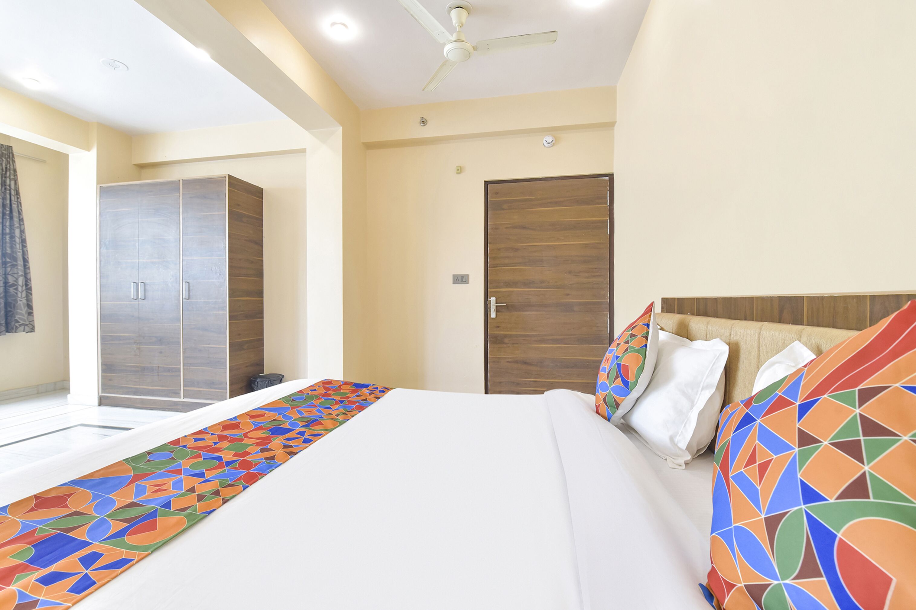 Quarto de hotel com cama, ventoinha no teto, guarda-roupa e porta.