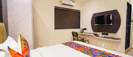 Quarto de hotel com cama, escrivaninha, cadeira, ar condicionado, televisão e porta.