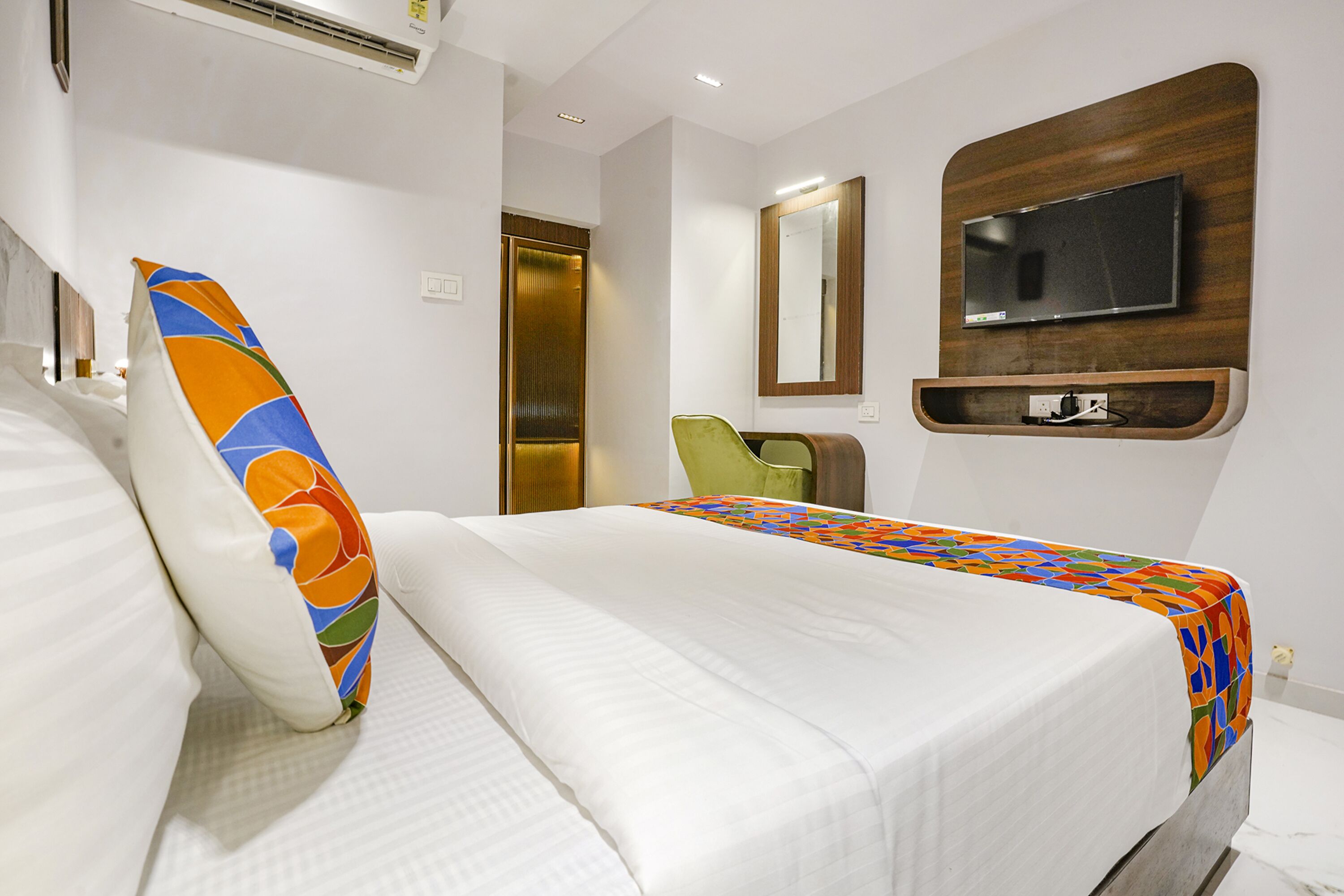 Quarto de hotel com uma cama, uma cadeira, uma televisão fixada na parede e uma porta.