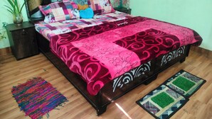 Quarto com cama, mesas de cabeceira, piso de madeira e tapete colorido.