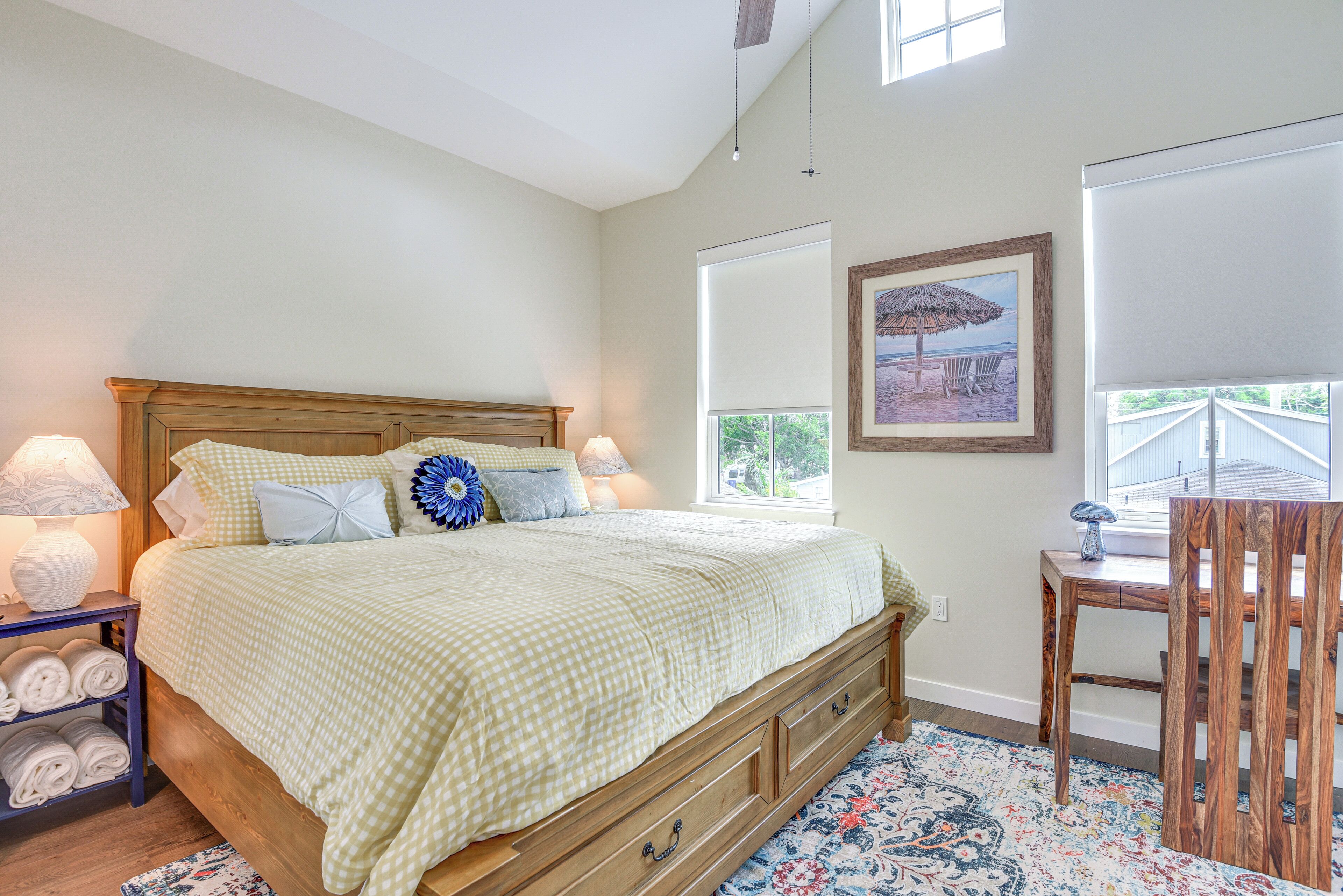 Quarto com cama grande, cabeceira de madeira, duas luminárias de cabeceira, uma cadeira, janela com vista e um quadro na parede.