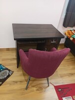 Uma escrivaninha de madeira com gavetas, uma cadeira vermelha e um tapete estampado sobre piso de madeira.