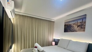 Quarto de hotel com cama, cortinas, um quadro e ar condicionado.