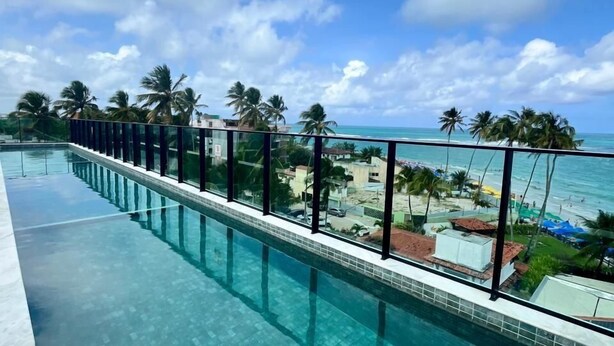Uma piscina infinita longa e transparente, com vista para o oceano e palmeiras.