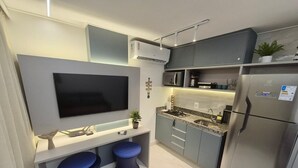 Uma cozinha moderna com TV integrada, armários cinza, geladeira de aço inoxidável e dois banquetes azuis.