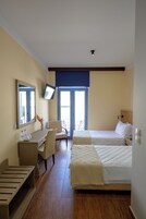 Quarto de hotel com duas camas, uma mesa, uma cadeira, uma televisão e vista para a varanda.