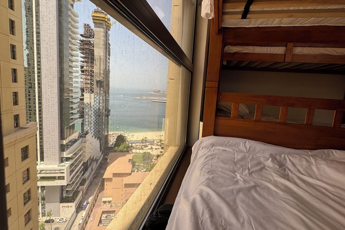 Quarto de hotel alto com uma grande janela com vista para a paisagem urbana e a praia.