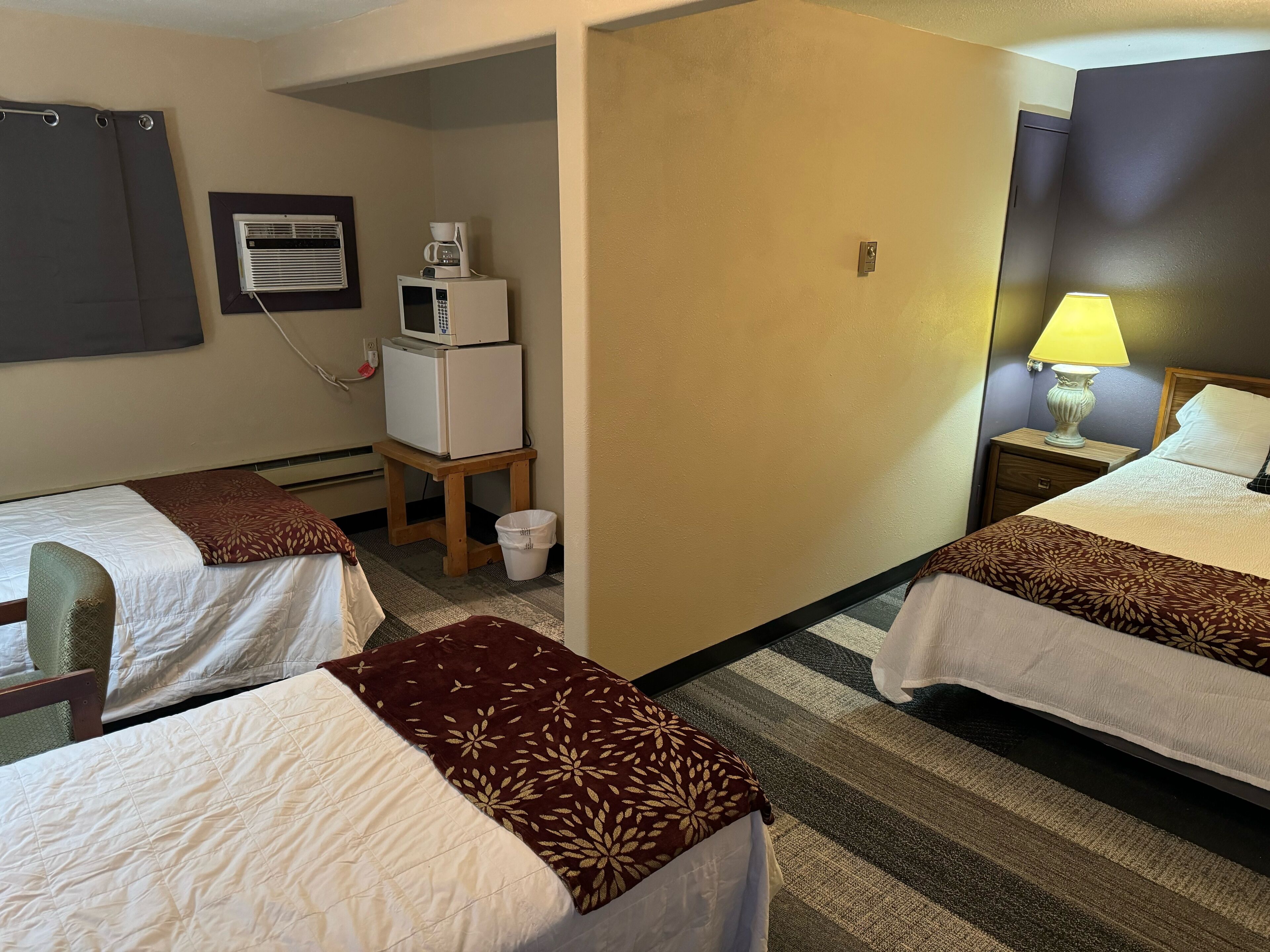 Quarto de hotel com duas camas, micro-ondas, uma mesinha, um cesto de lixo e uma luminária em uma mesinha de cabeceira.