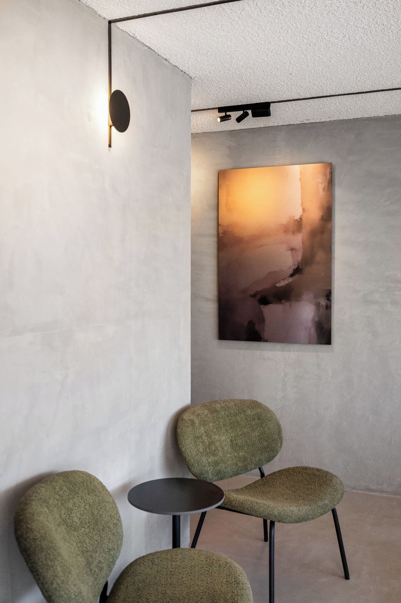 Um interior moderno com design minimalista, apresentando uma parede de concreto, uma mesa redonda e duas cadeiras estofadas.