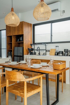 Uma cozinha moderna com armários de madeira, uma mesa de jantar posta com pratos e copos brancos, e uma grande janela que traz luz natural.