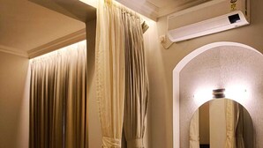 Quarto de hotel com um espelho grande, uma mesa de toucador com um banquinho e uma janela com cortina.