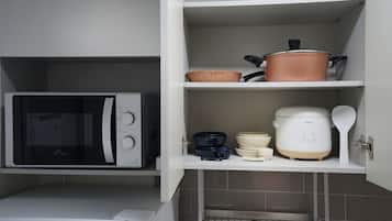 Uma cozinha com micro-ondas, panela de arroz e diversos recipientes e panelas.
