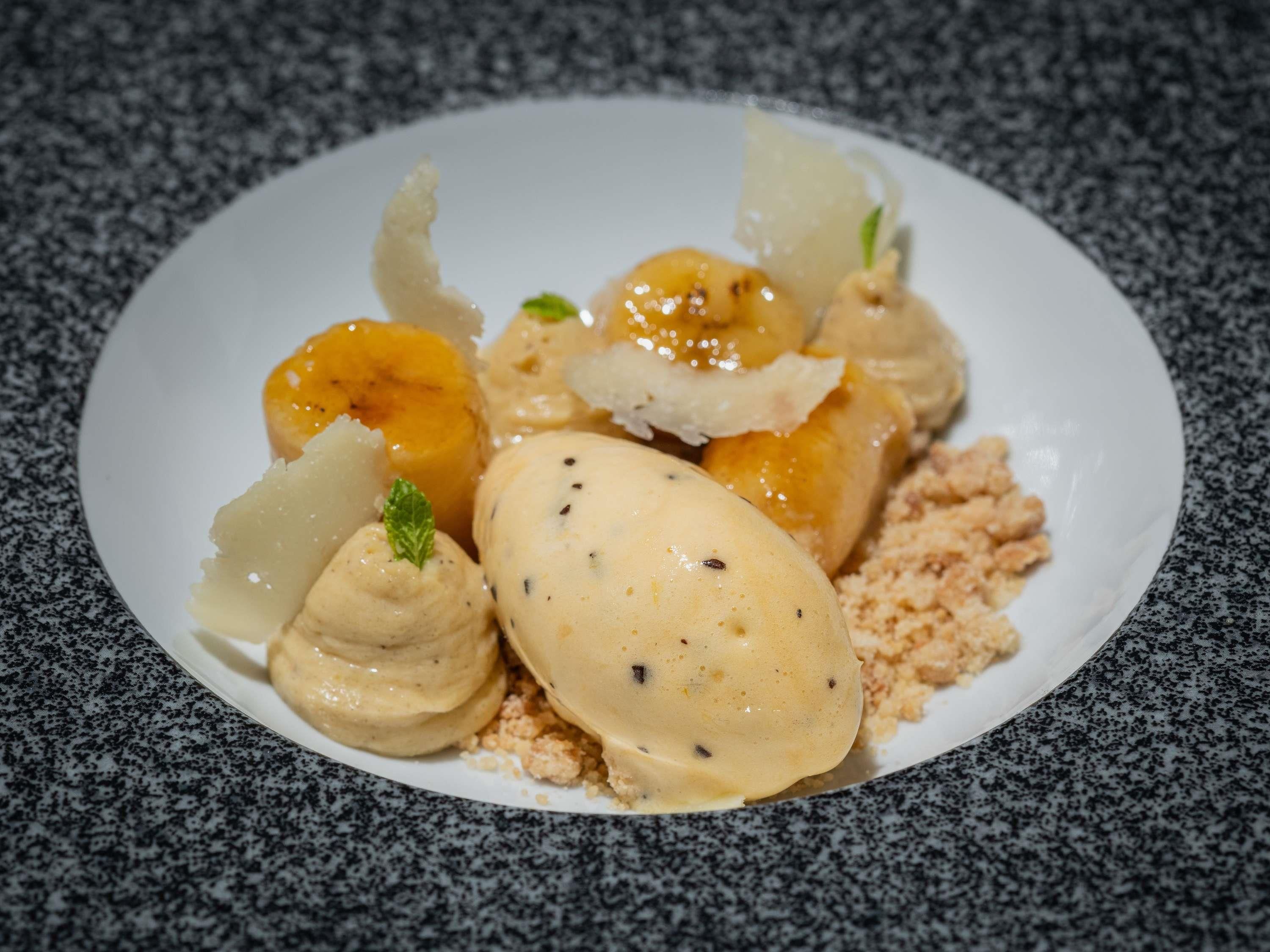 Prato de sobremesa com sorvete, fruta e crumble em bancada salpicada.
