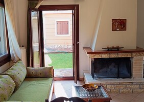 Uma sala de estar com sofá, lareira e vista para uma casa através de uma porta aberta.