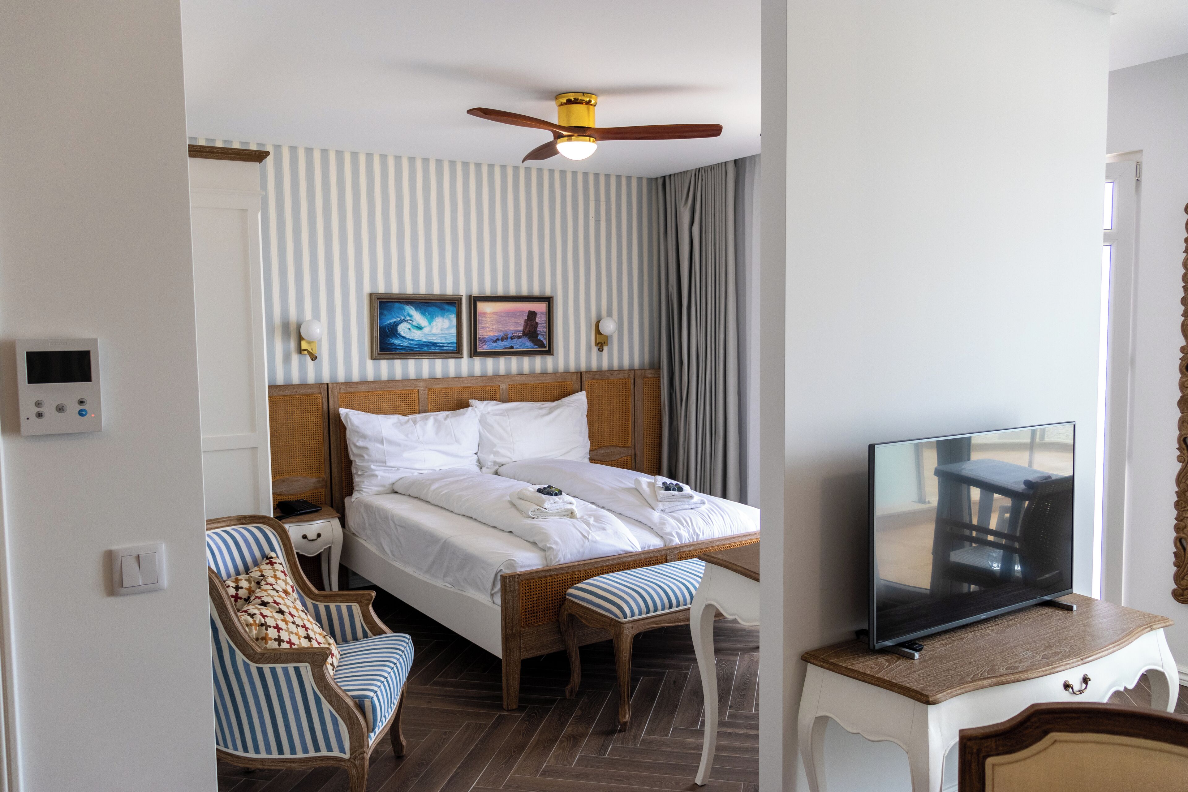 Quarto de hotel com cama, televisão, ventoinha no teto e papel de parede listrado.