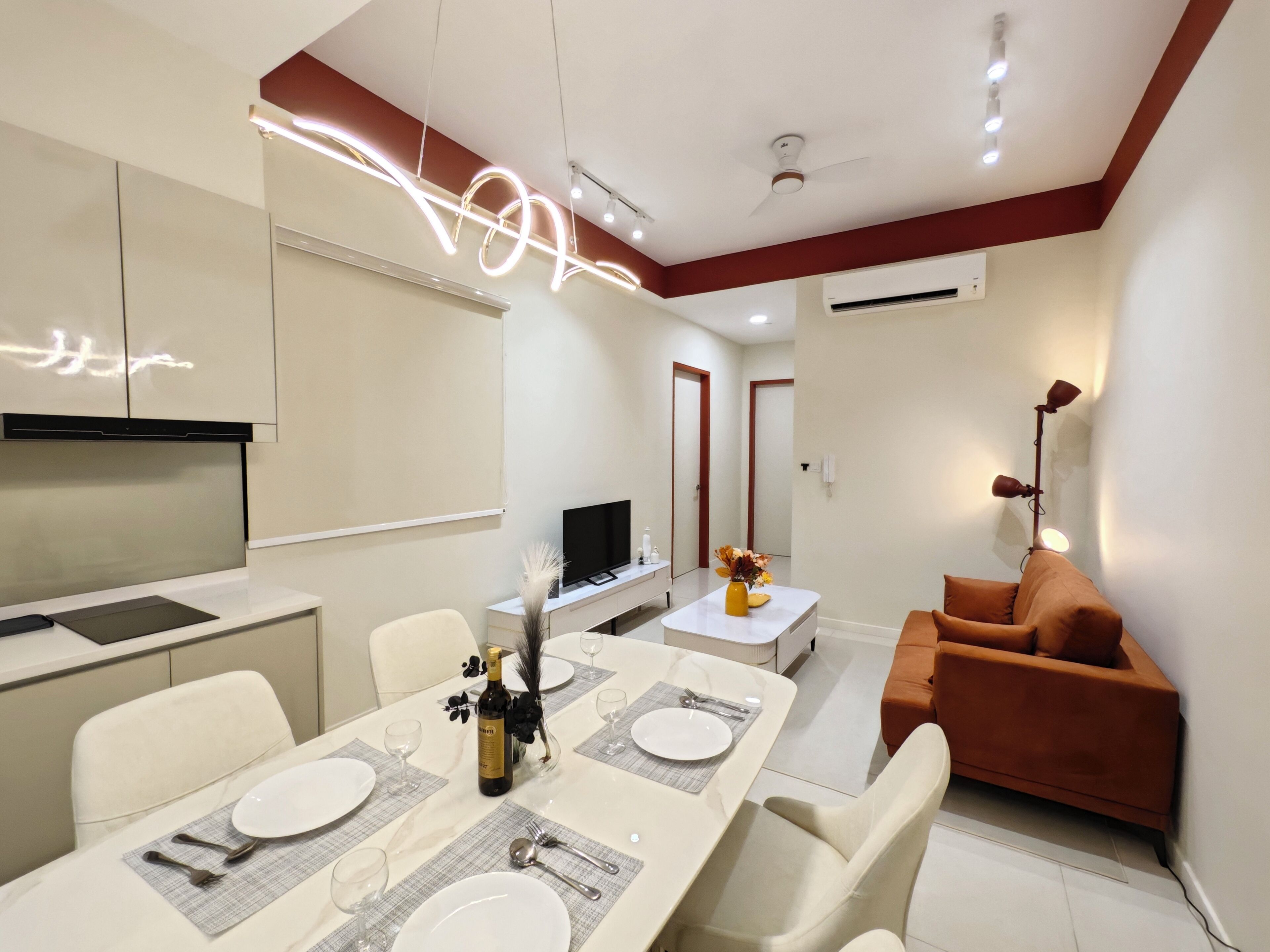 Uma sala de jantar moderna com uma mesa posta para dois, um sofá e uma televisão ao fundo.