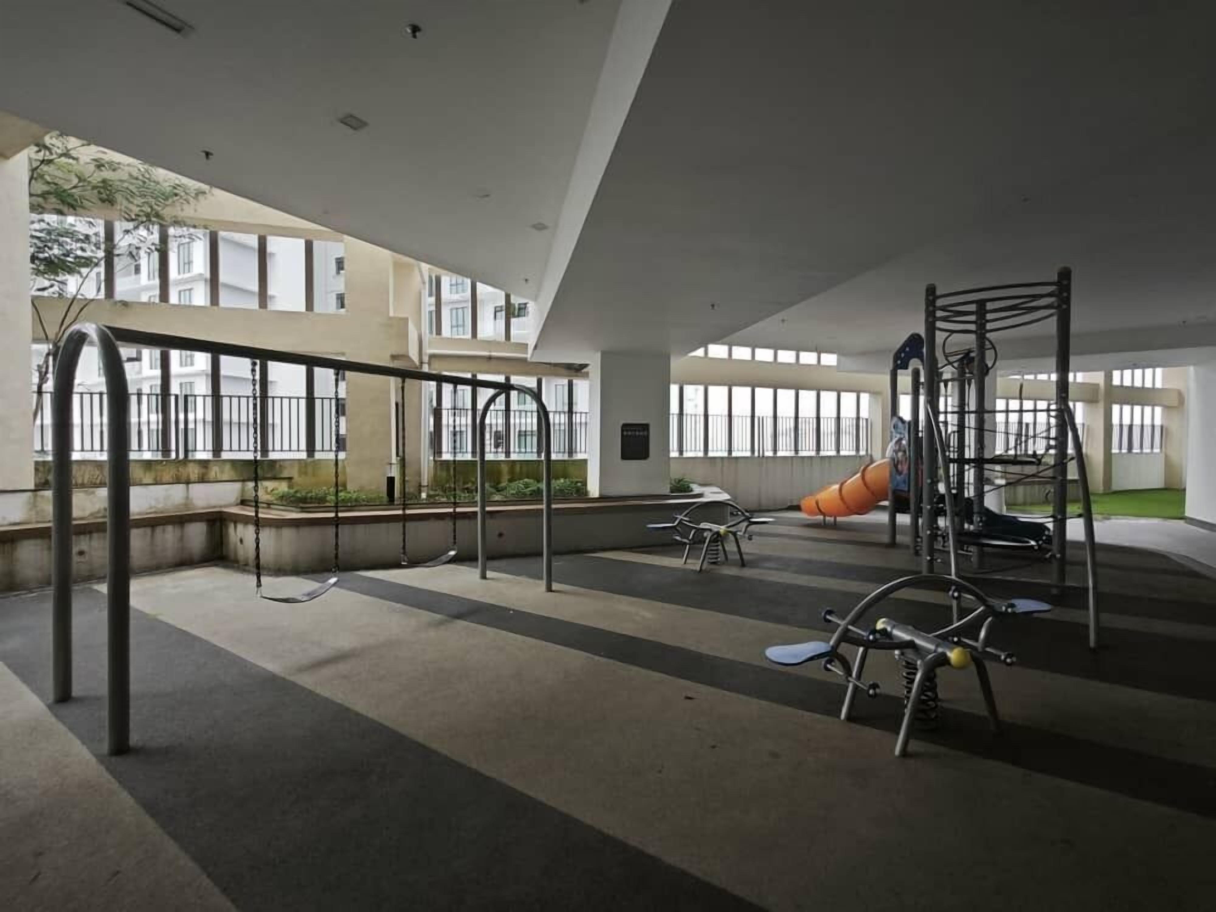 Uma área de recreação interna ampla, com diversos equipamentos de exercícios, incluindo balanços e um escorrega, e grandes janelas que proporcionam iluminação natural.