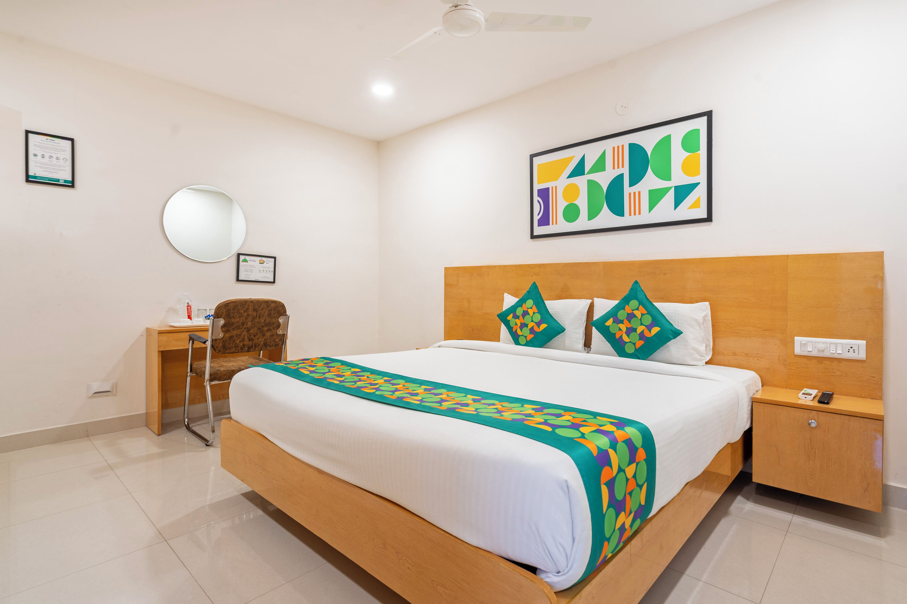 Quarto de hotel com cama, mesa de cabeceira, cadeira e ventoinha no teto.