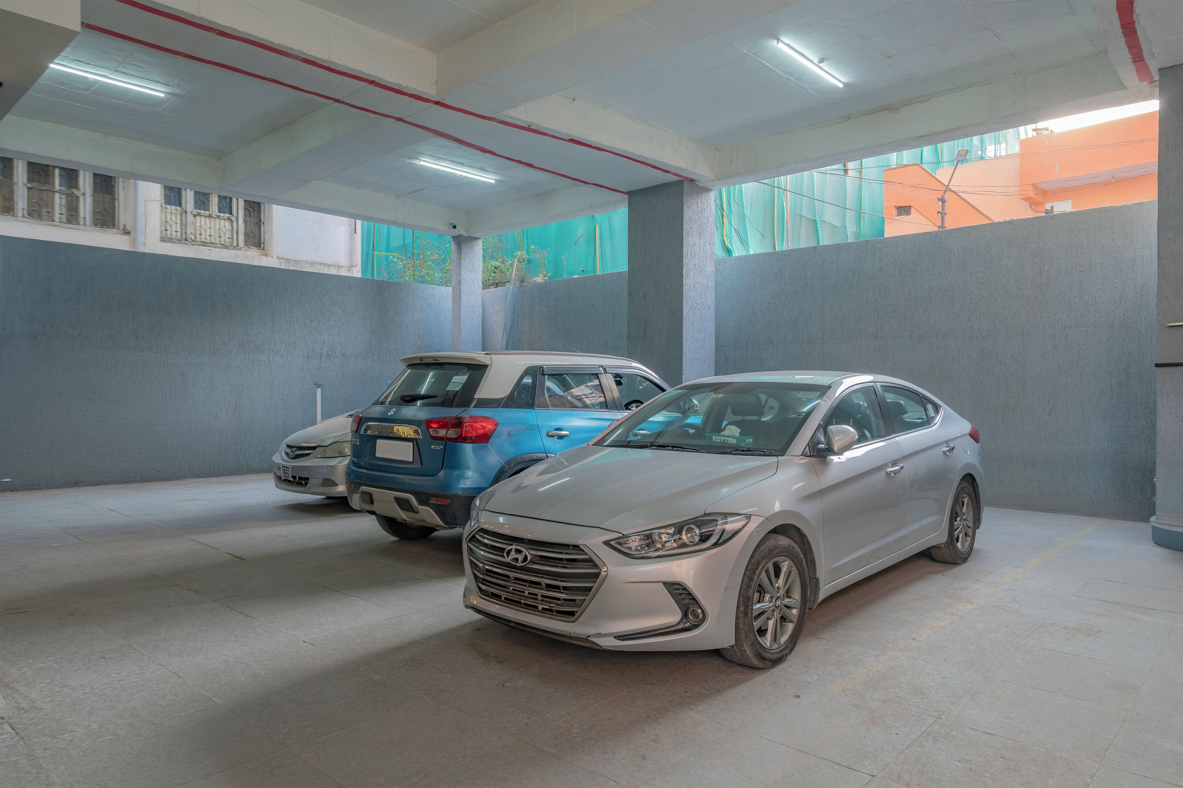 Garagem de estacionamento com dois carros, paredes de concreto e teto com lâmpadas fluorescentes.