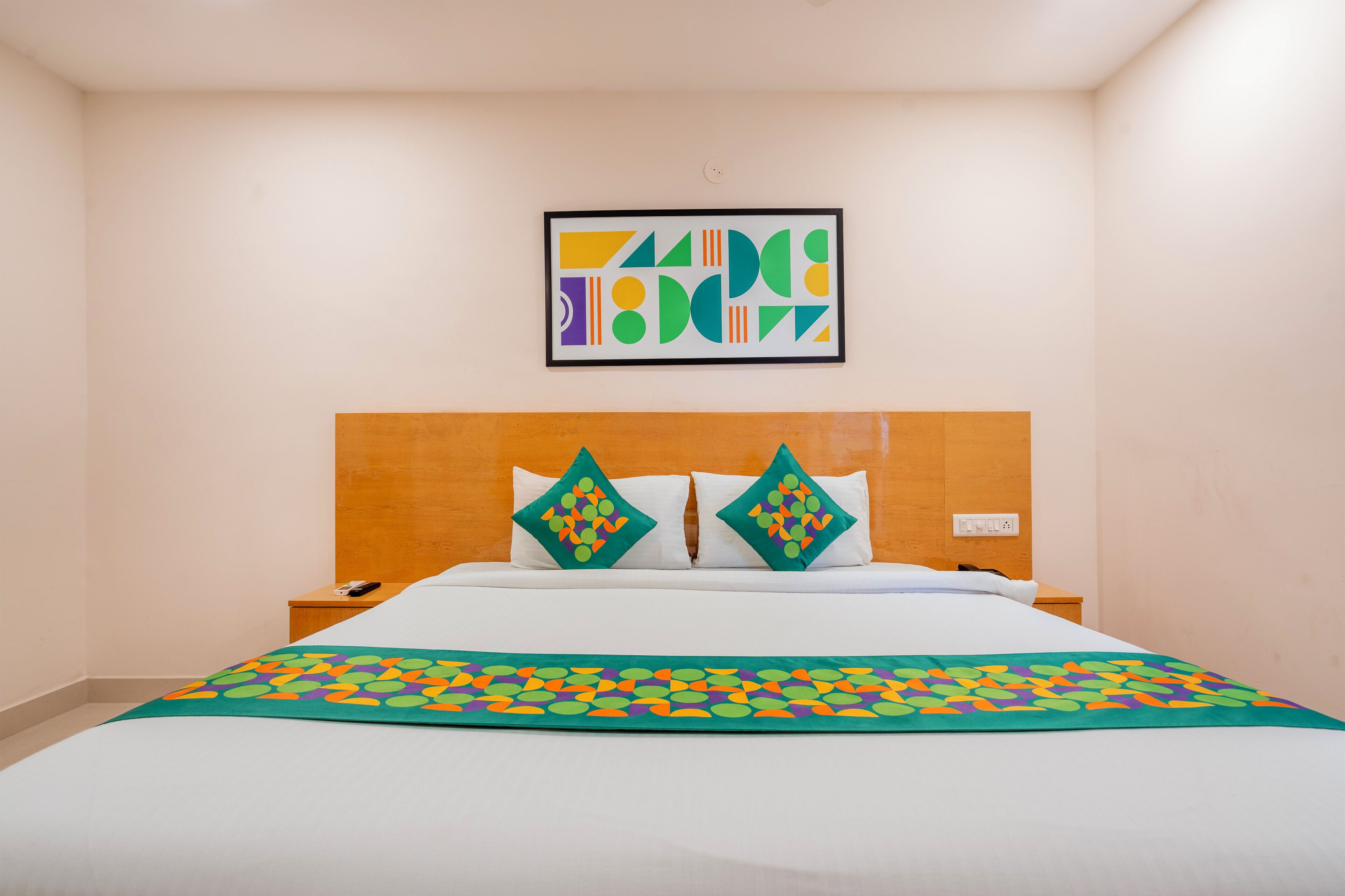 Quarto de hotel com cama, cabeceira, obra de arte pendurada na parede e colcha estampada.