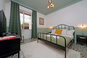 Quarto com cama, escrivaninha, cadeira, janela com cortinas, um quadro e luminária no teto.