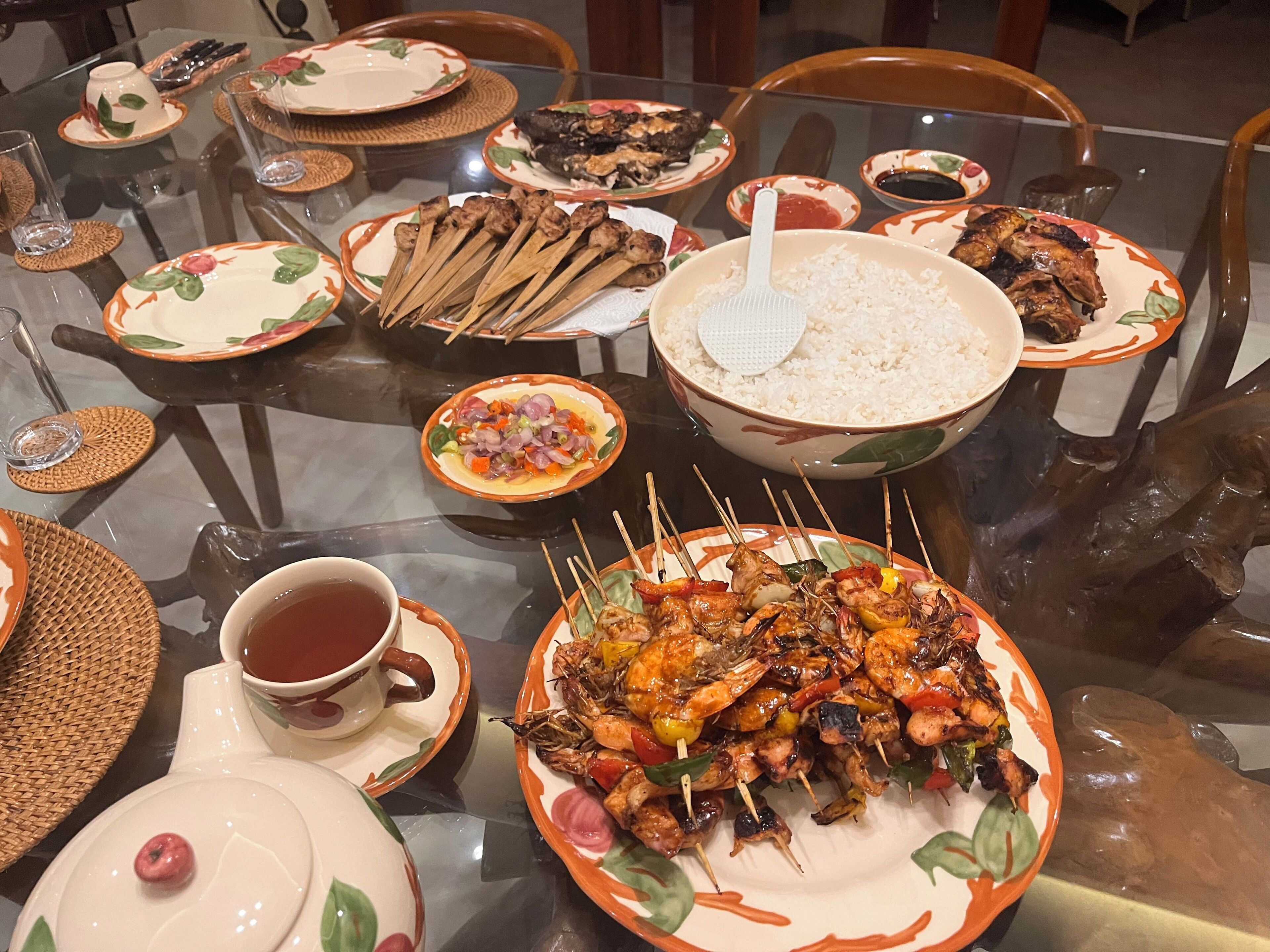 Uma mesa de jantar posta com diversos pratos, incluindo espetinhos, arroz e uma tigela de sopa.