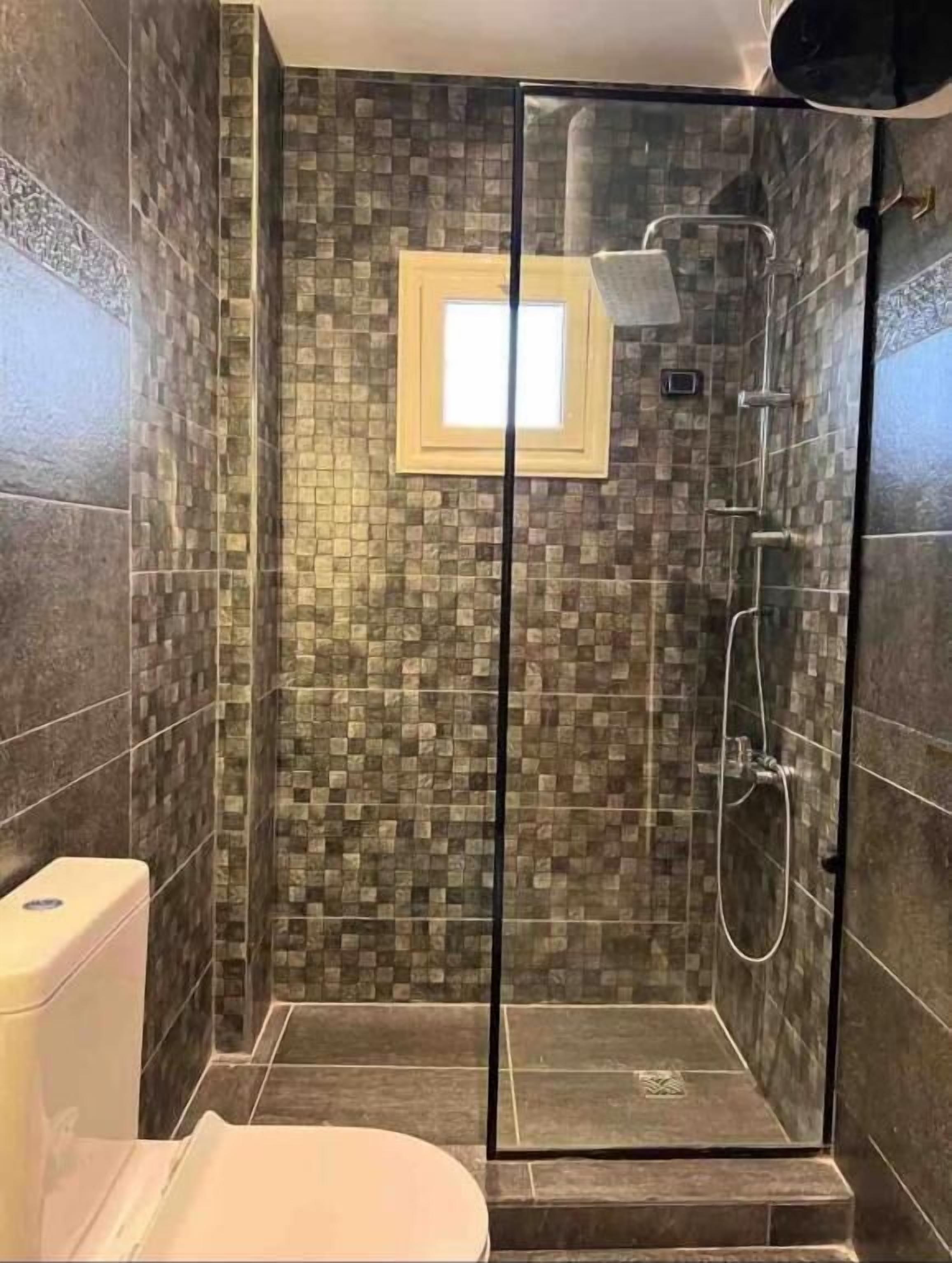 Um chuveiro sem barreiras com porta de vidro, paredes revestidas de azulejos e uma pequena janela.