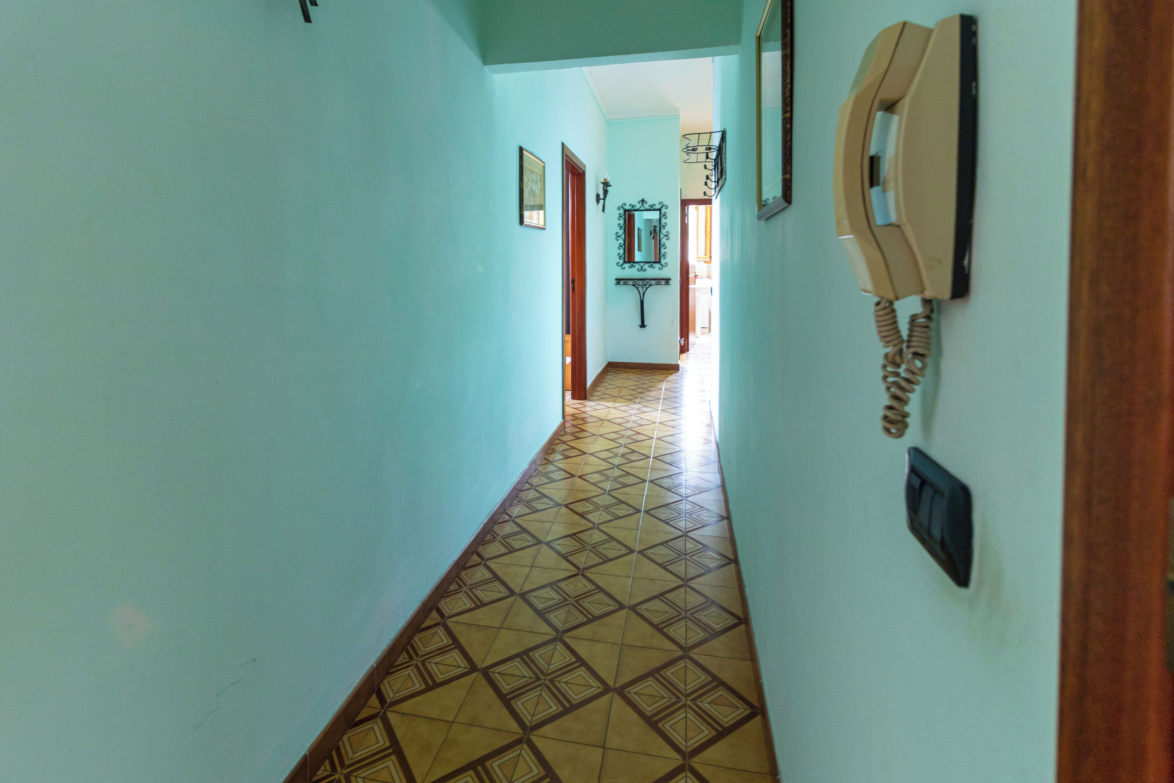 Um corredor com ladrilhos estampados no chão, paredes azul claro e um telefone na parede.