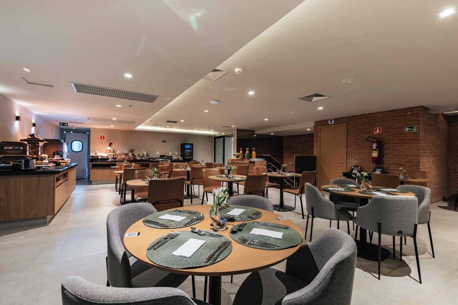Uma sala de jantar moderna com mesas redondas, cadeiras e cozinha ao fundo.