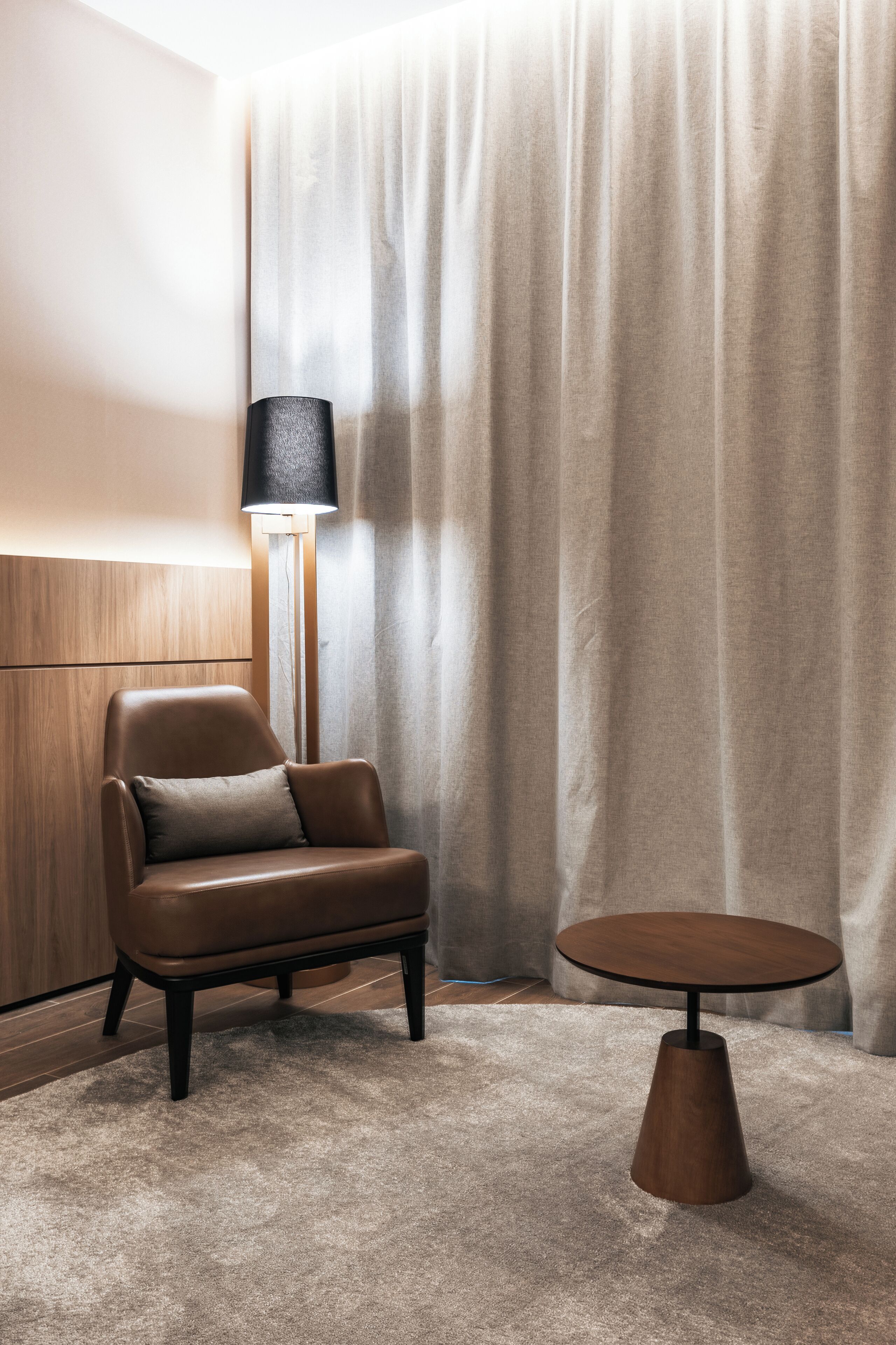 Quarto moderno com poltrona de couro, mesa redonda de madeira e luminária de chão.