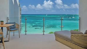 Uma varanda com vista para o oceano e barcos, um sofá de vime, uma mesa com uma planta e uma cadeira.