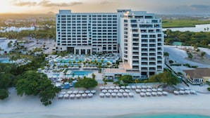 Resort com um edifício grande, várias piscinas e área de praia com guarda-sóis e espreguiçadeiras.