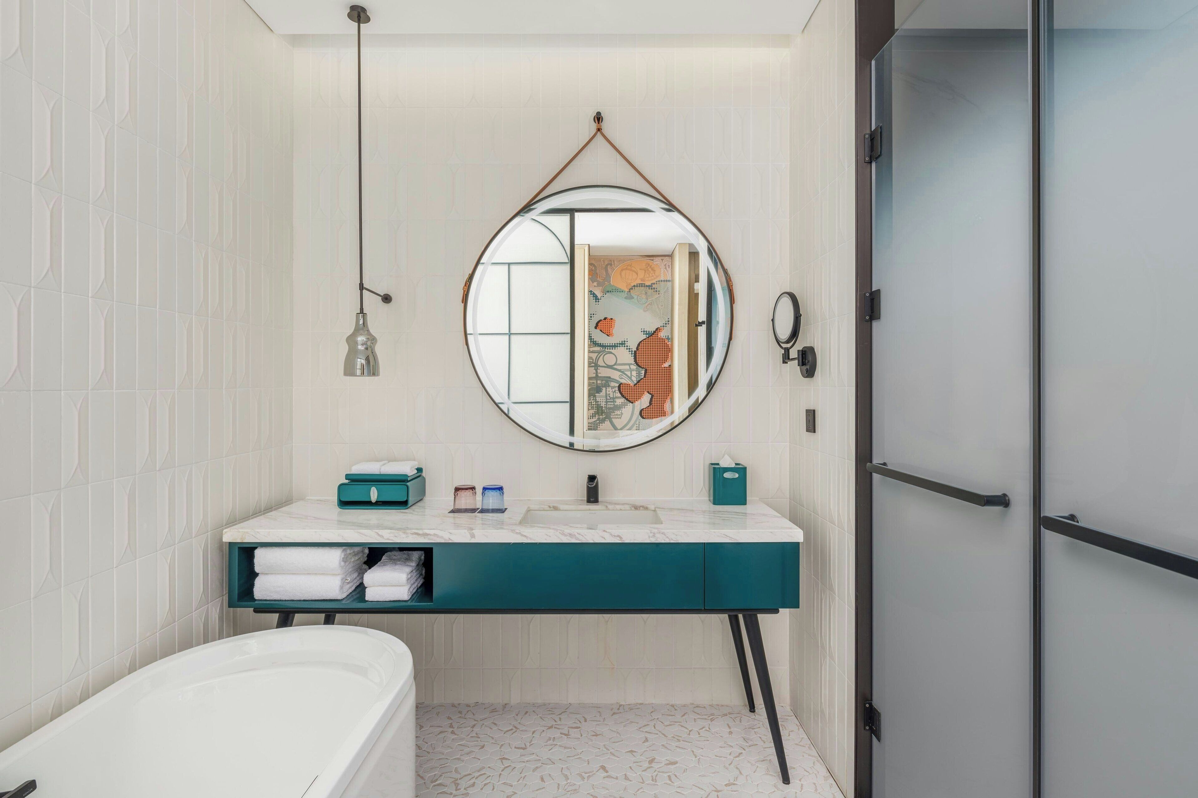 Casa de banho moderna com uma banheira independente, um espelho redondo e um design de parede geométrico, e um lavatório azul-turquesa com bancada de mármore.