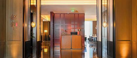 Um saguão de hotel moderno com piso refletivo, balcão de recepção e divisória decorativa com caracteres chineses.