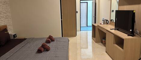 Quarto de hotel moderno com cama, televisão, escrivaninha e banheiro visível por uma porta aberta.