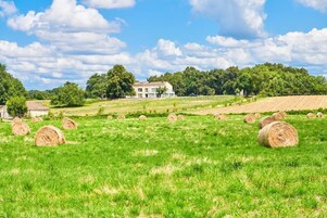 Paisagem rural com uma casa grande cercada por campos e fardos de feno.