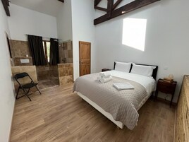 Quarto com uma cama grande, piso de madeira, área de chuveiro e porta de madeira.