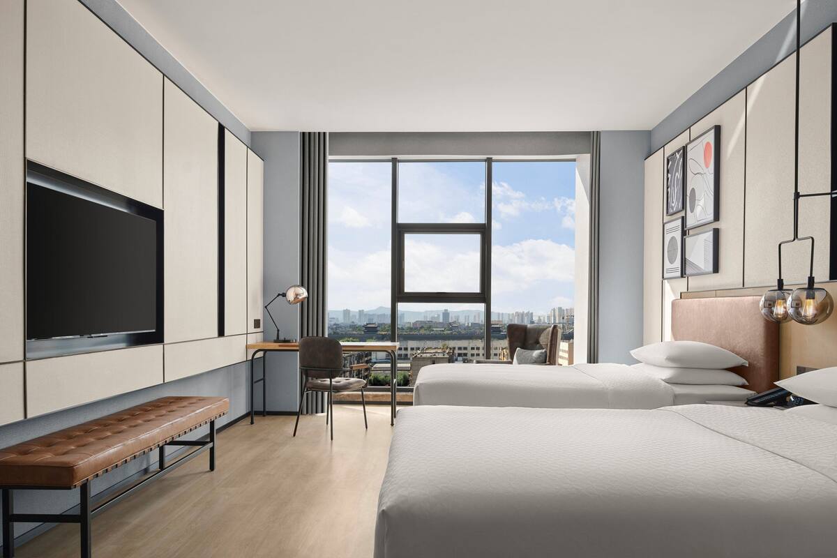 Quarto de hotel moderno com uma janela ampla, televisão de tela plana, uma escrivaninha e duas camas.