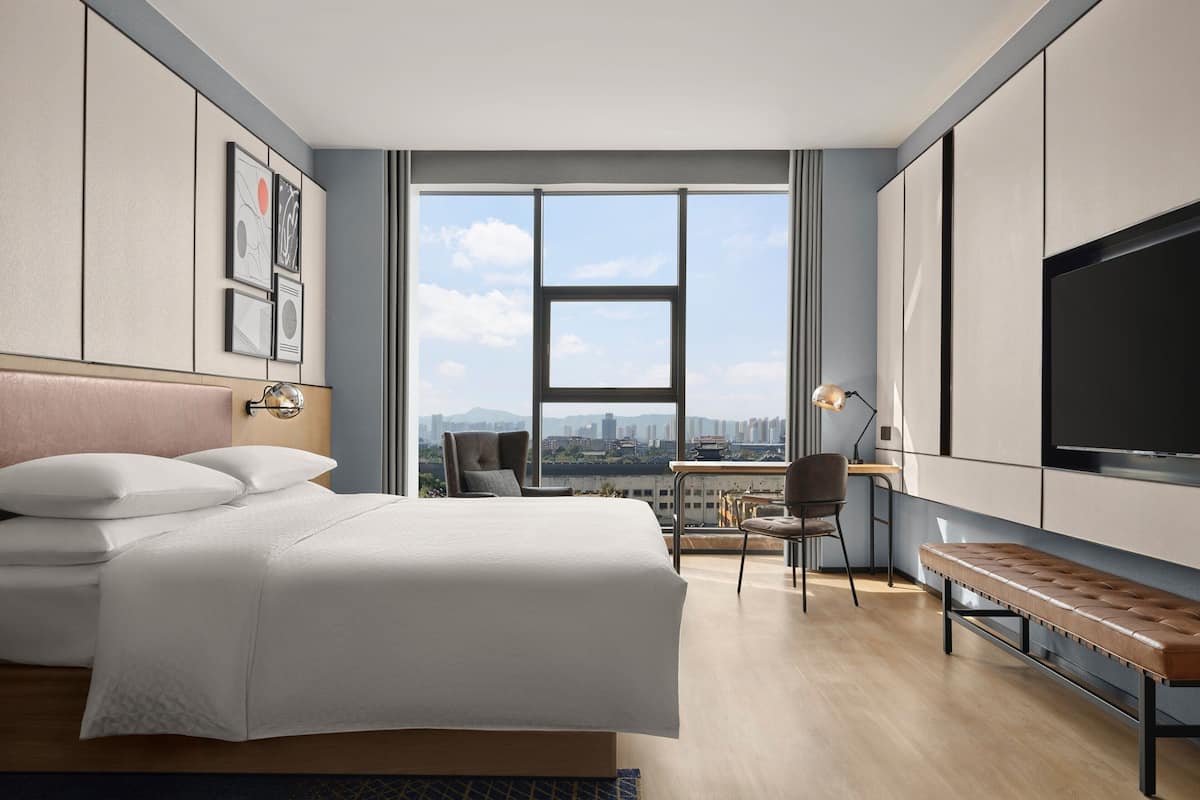 Quarto de hotel moderno com uma cama grande, uma escrivaninha, uma cadeira e uma televisão.