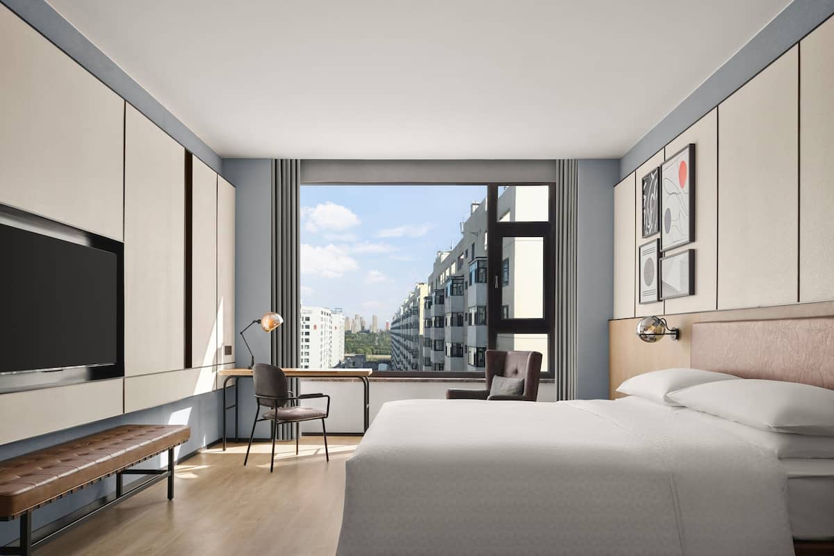 Quarto de hotel moderno com uma cama grande, uma escrivaninha, uma cadeira e uma televisão.